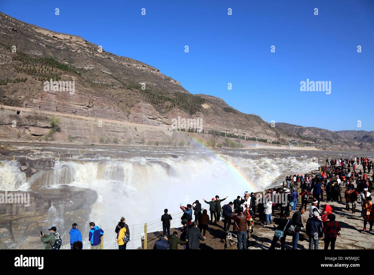 Tourists enjoy the scenery of a rainbow over the Hukou Waterfall of the ...