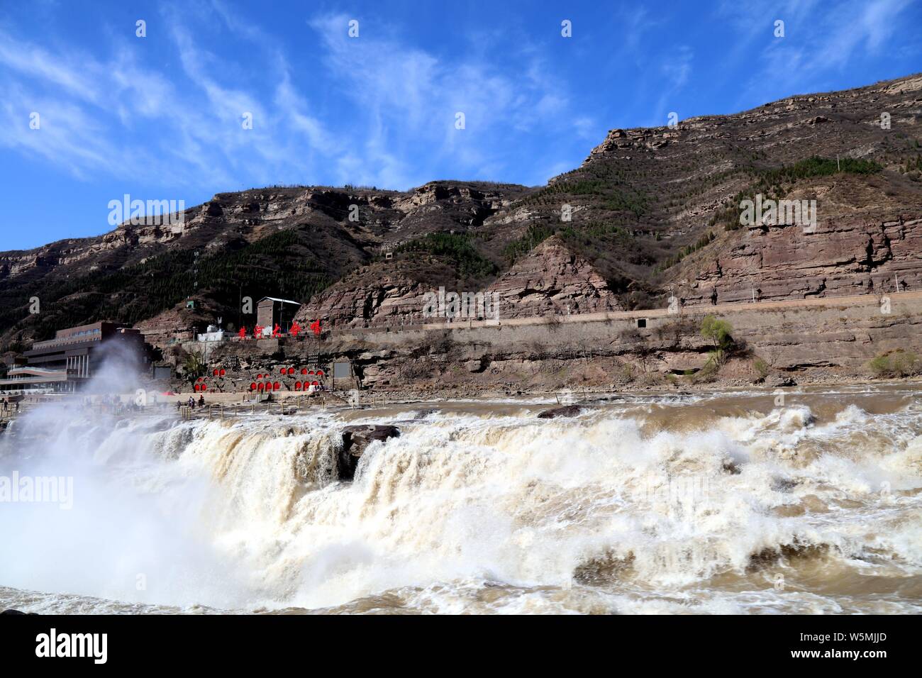 Tourists enjoy the scenery of a rainbow over the Hukou Waterfall of the ...