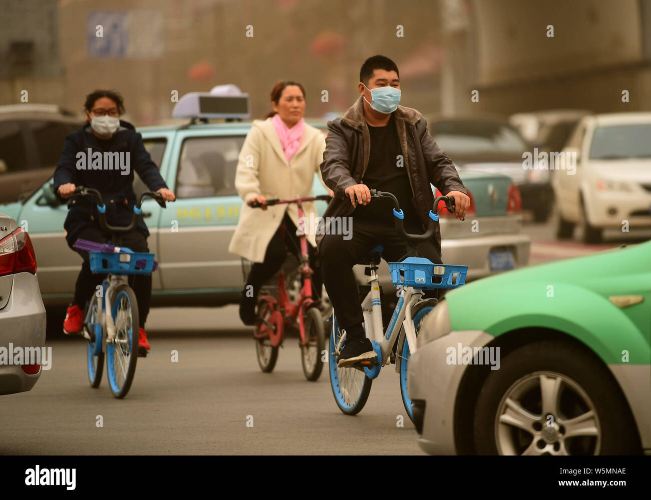 Cyclists cover their mouths against air pollution as they ride on a ...