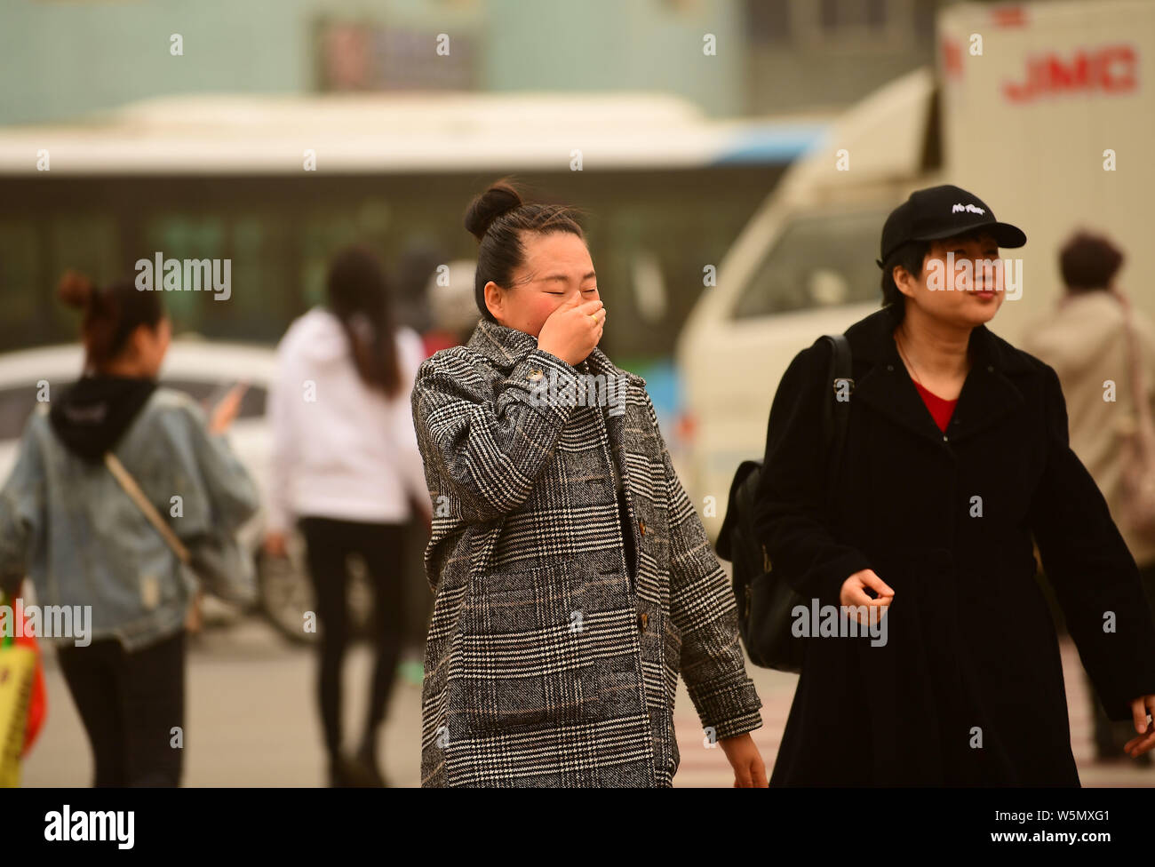 A pedestrian covers her mouth against air pollution as she walks on a ...