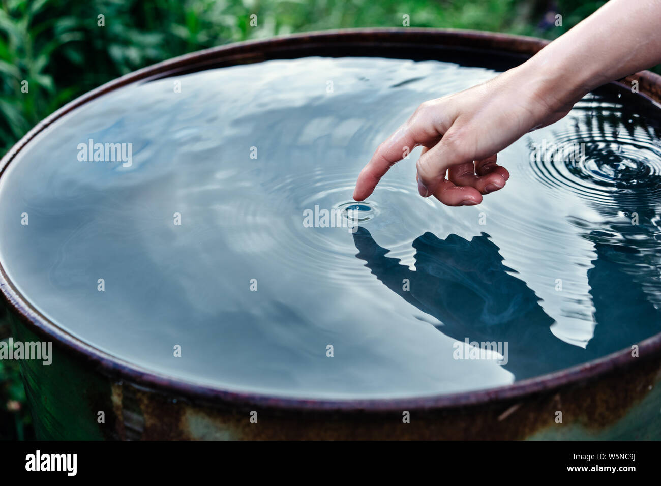 Wet female hand touches clean water in a barrel forming circles on the ...