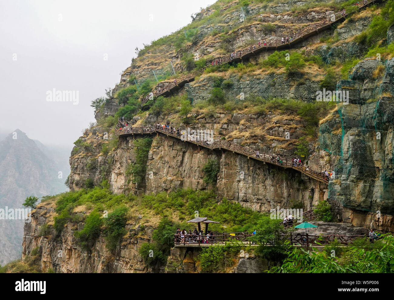 Tourists walk on a zigzag cliff road around a mountain at the Shidu ...