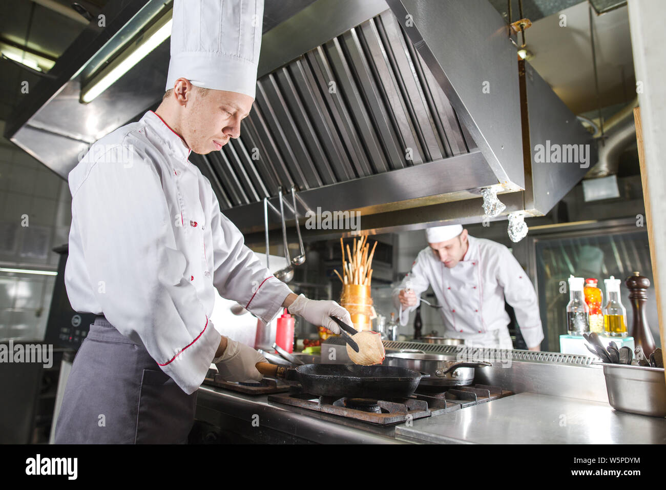 Chef in restaurant kitchen at stove with pan, cooking Stock Photo - Alamy