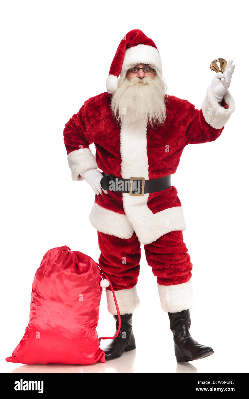 saint nick holding bell stands with hand on hip near presents bag on ...