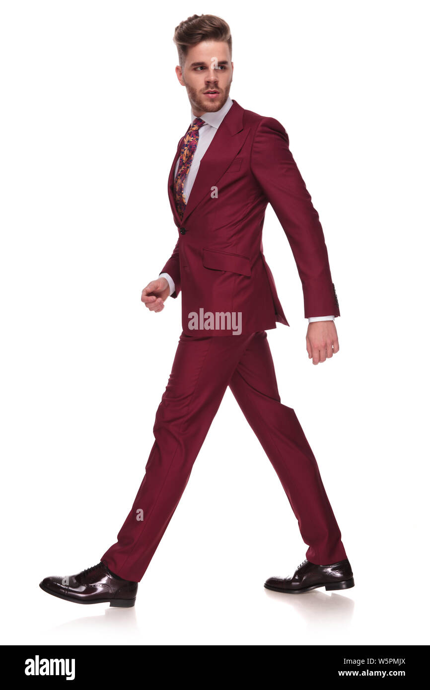 side view of confident businessman in grena suit walking on white ...