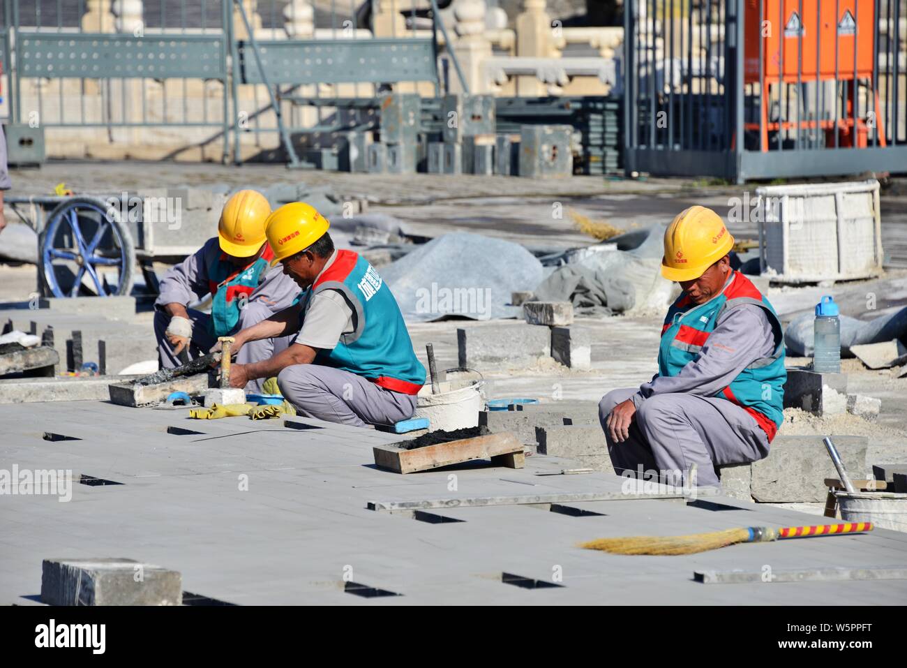 Chinese construction workers renovate the ground of the square in front ...