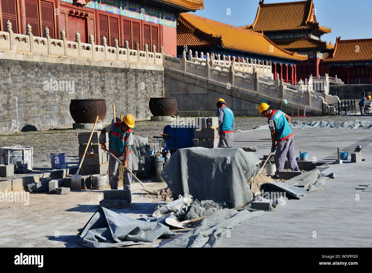 Chinese construction workers renovate the ground of the square in front ...
