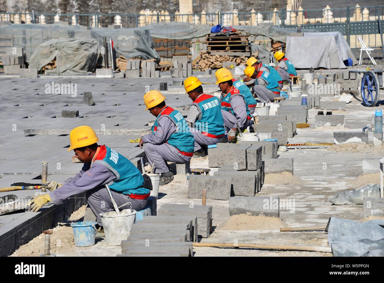 Chinese construction workers renovate the ground of the square in front ...