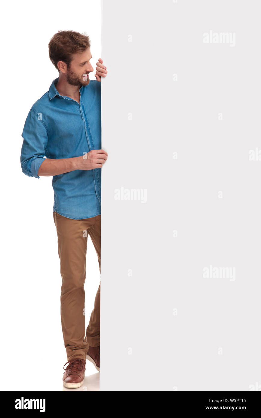 smiling casual man standing behind big blank billboard and showing it ...