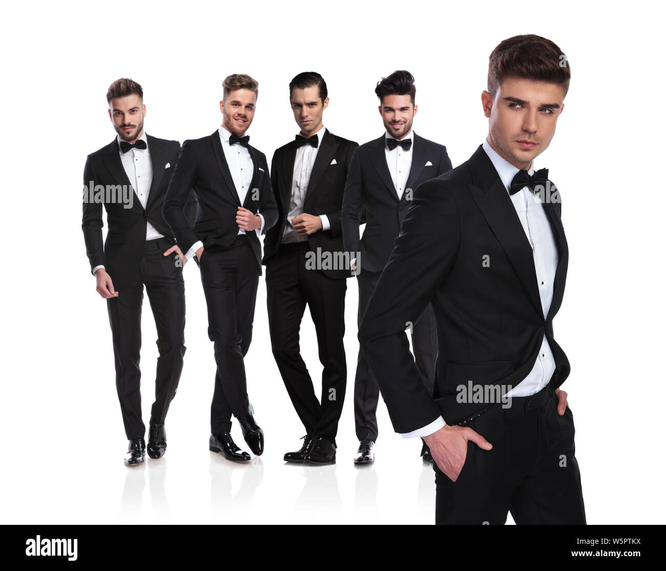 elegant team leader dressed in black tux stands in front with hands on ...