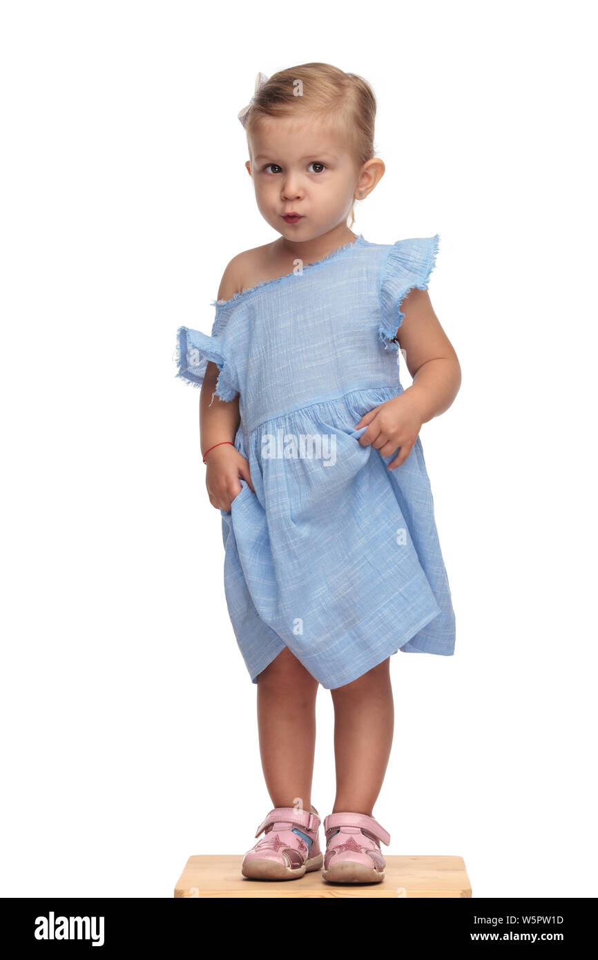 little girl makes a funny face while standing and pulling her dress on ...