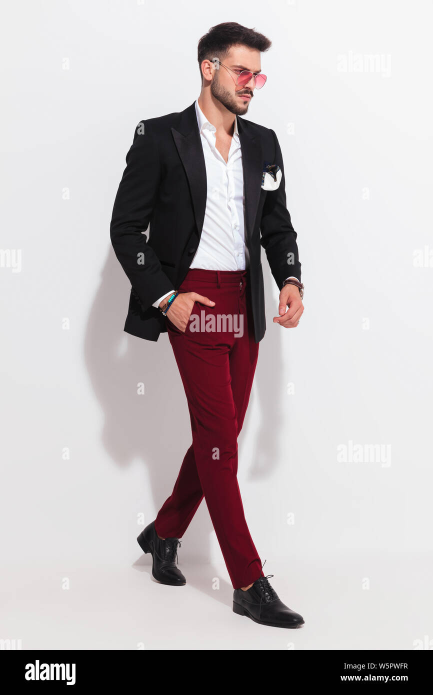 elegant man wearing undone black suit and yellow sunglasses walking to ...