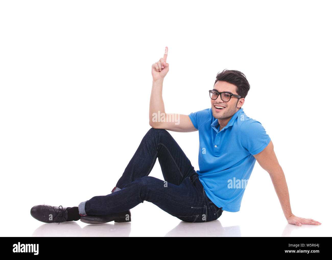 casual young man lying on the floor is pointing up at something on ...
