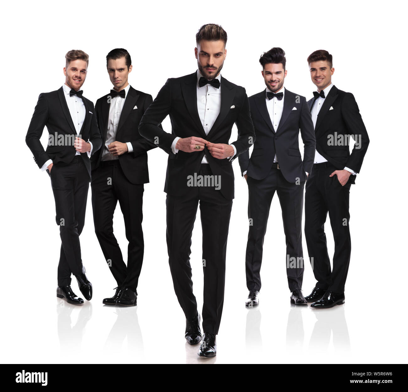 group of five elegant men wearing black tuxedoes with leader buttoning ...