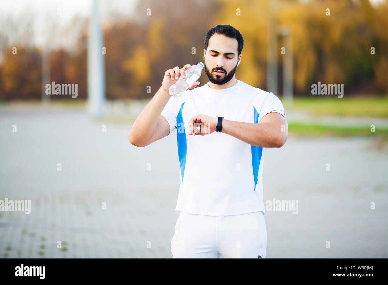 Exhausted runner man drink water on the park after workout Stock Photo ...