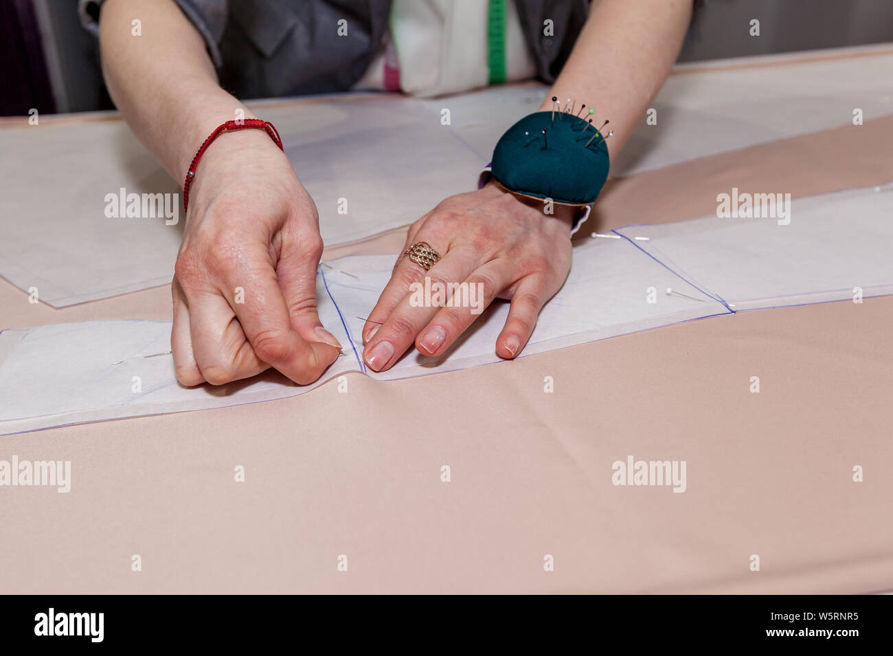 Female tailor hands with cloth, pattern and needle in the workshop ...