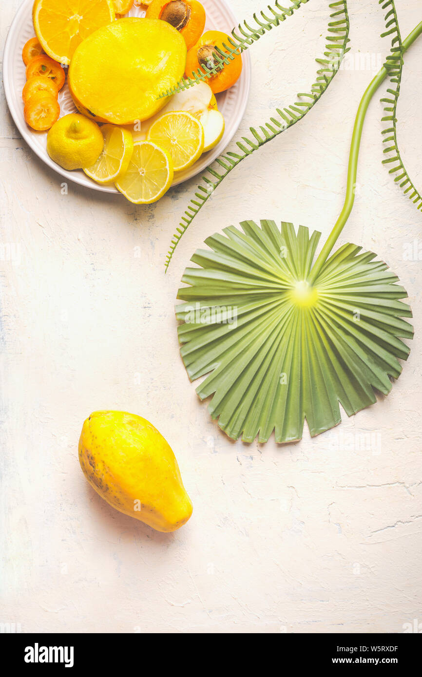 Whole papaya fruit on white table with tropical leaves and plate with ...
