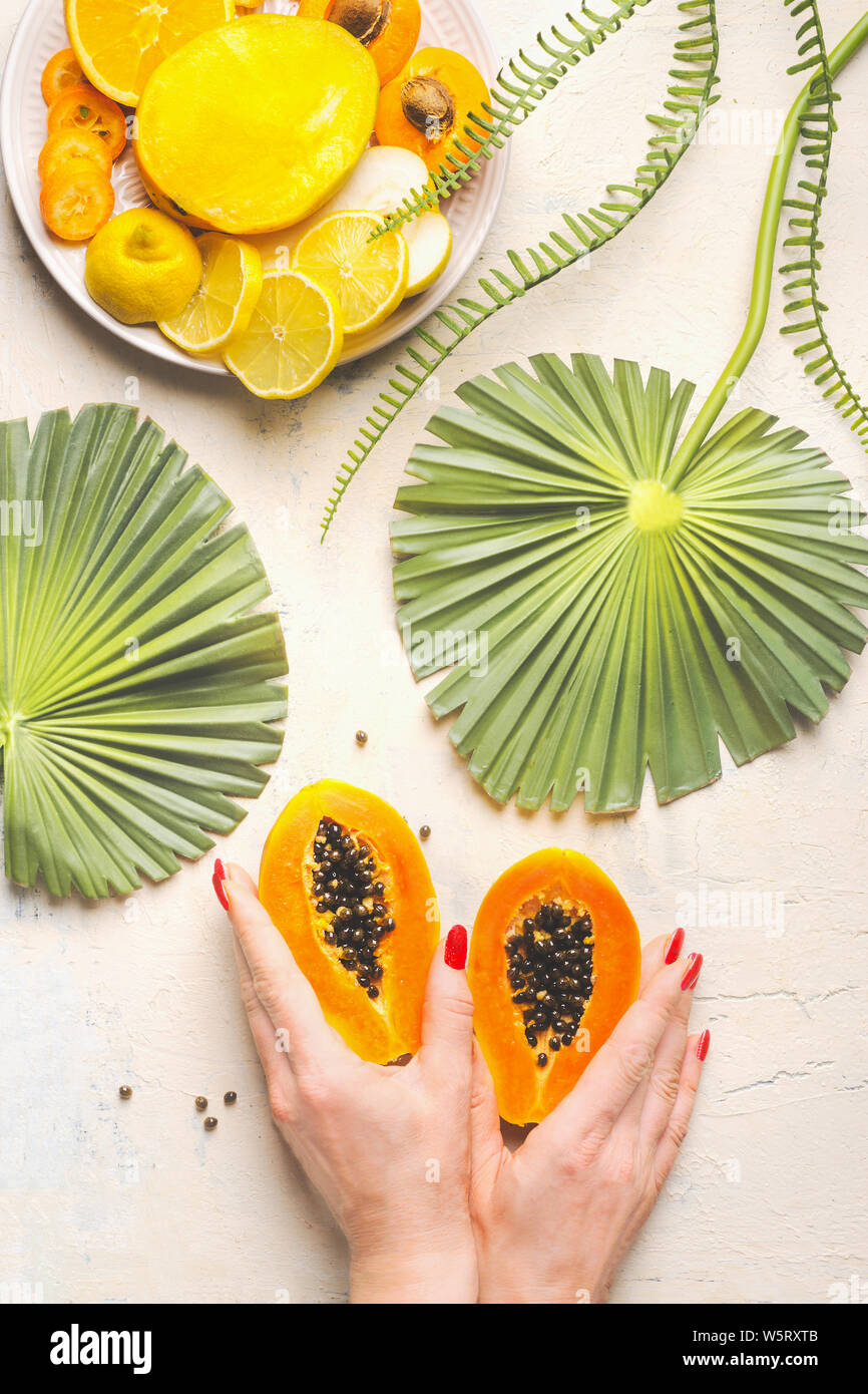 Female hands holding halved papaya fruit on white table with tropical ...