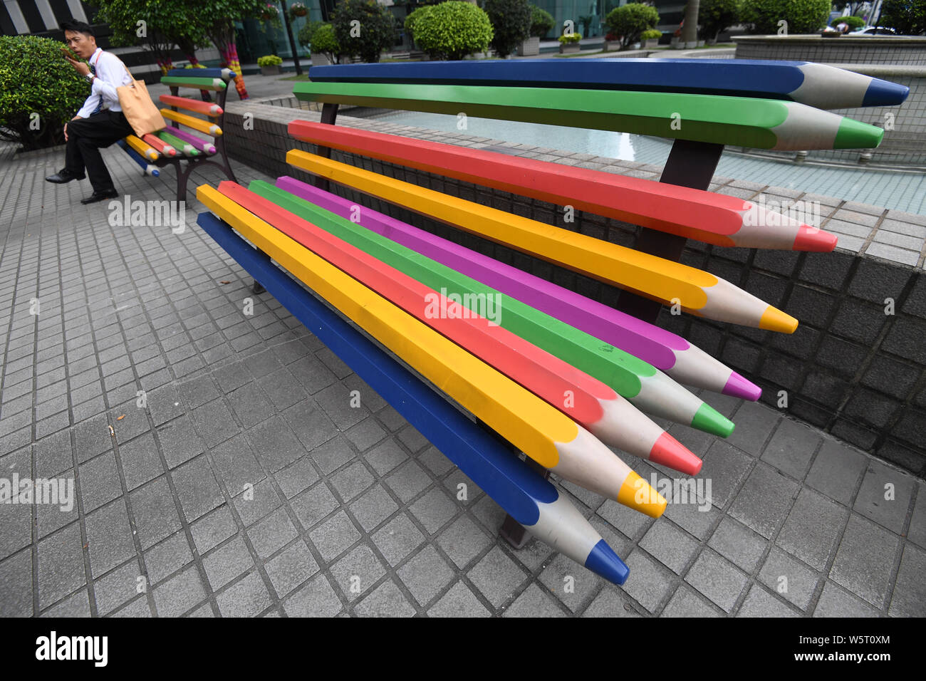 A Chinese man sits on a colored pencil bench next to others at a square ...