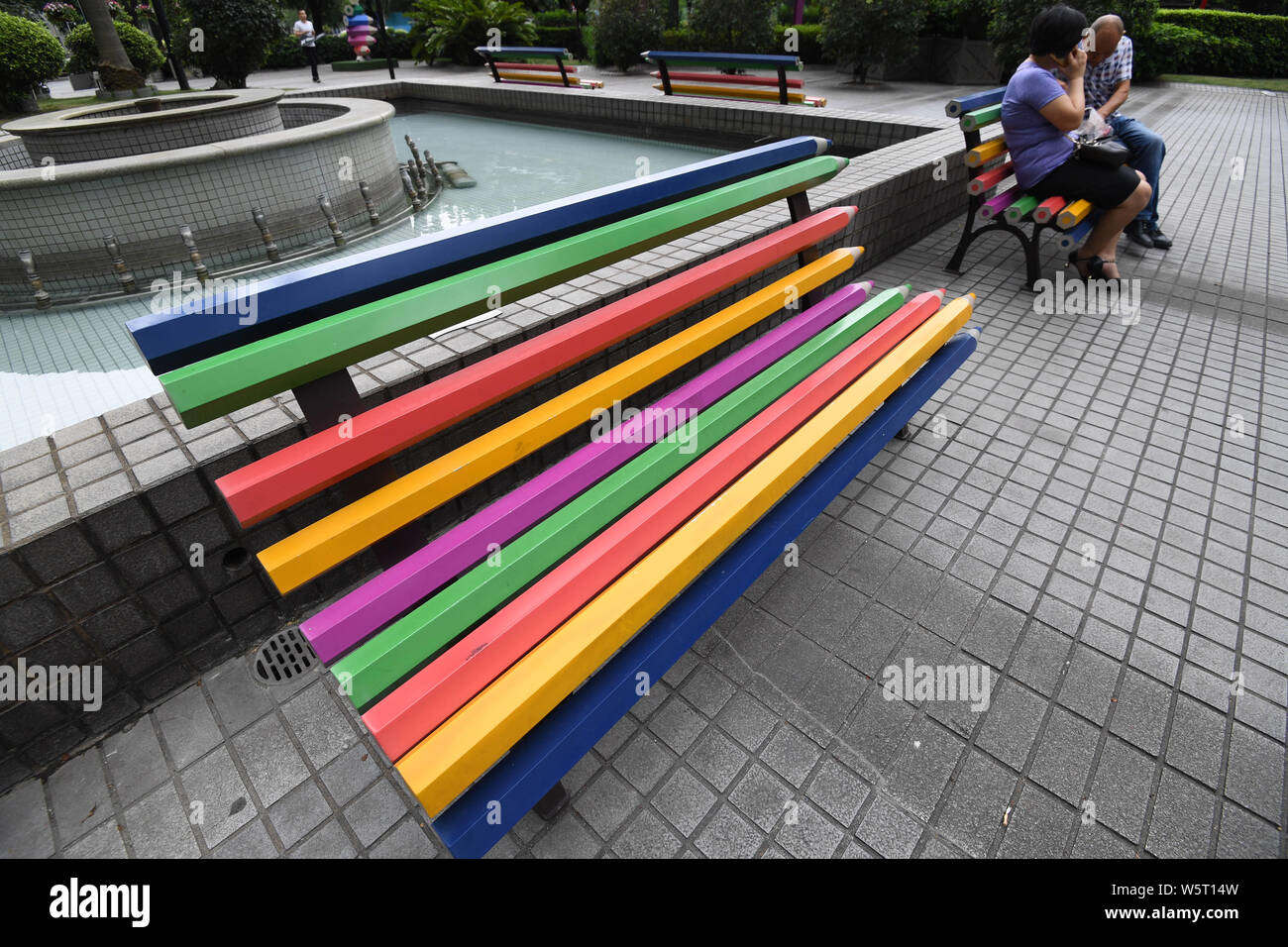 An elderly Chinese couple sits on a colored pencil bench next to others ...