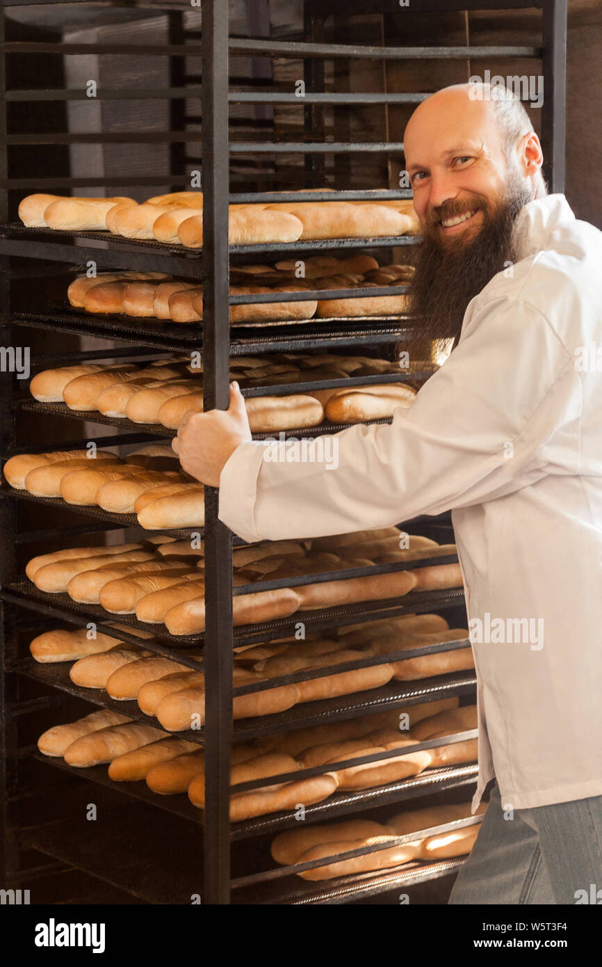 Portrait of pleasure young adult baker with long beard in white uniform ...