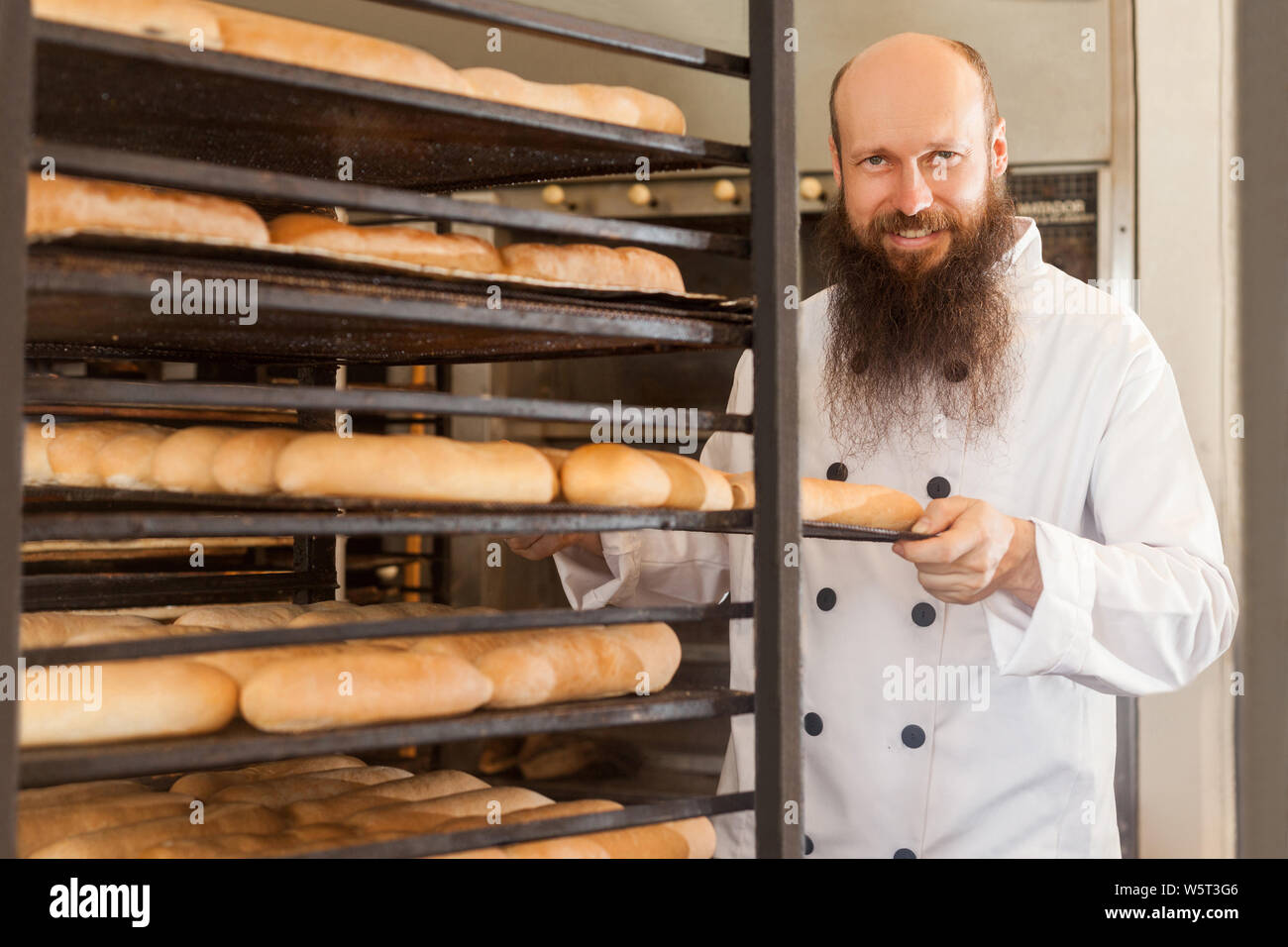 Portrait of smiling adult baker with long beard in white uniform ...