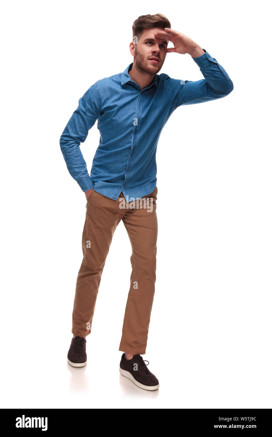 curious casual man looking to side in the distance making a hand visor ...