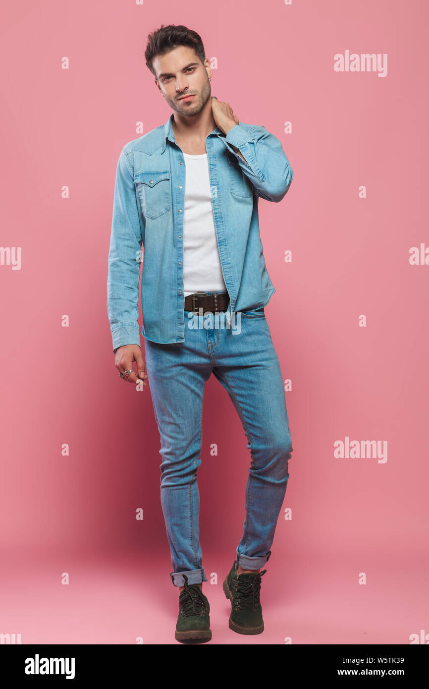 handsome man wearing undone denim shirt and jeans standing near a pink ...