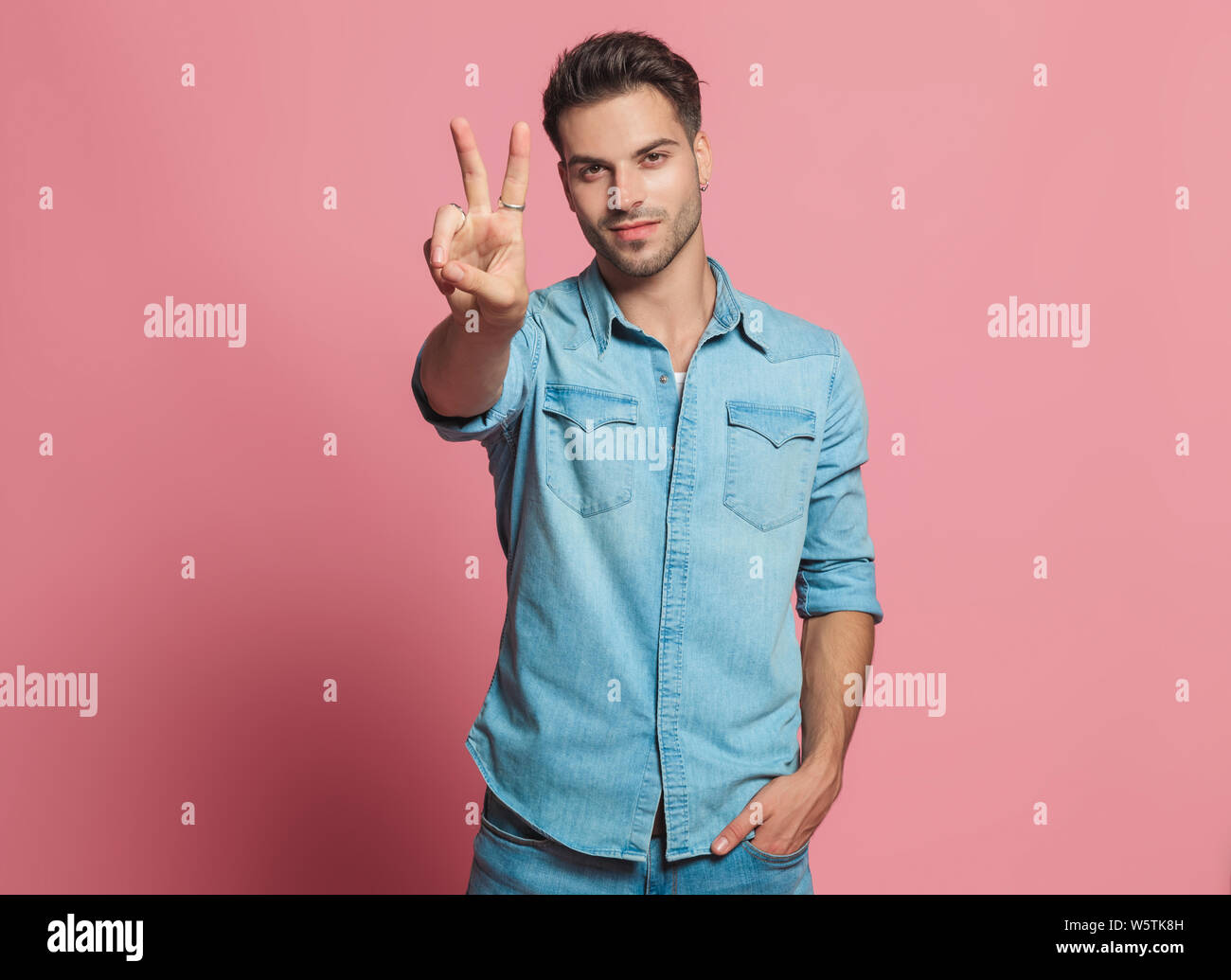 casual man makes peace sign while holding his pocket and standing on ...