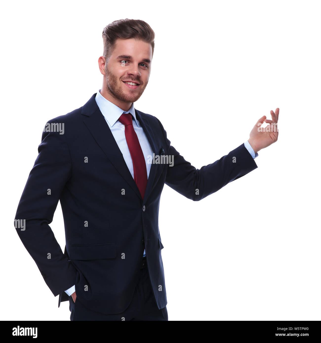 portrait of smiling young businessman presenting to side while standing ...