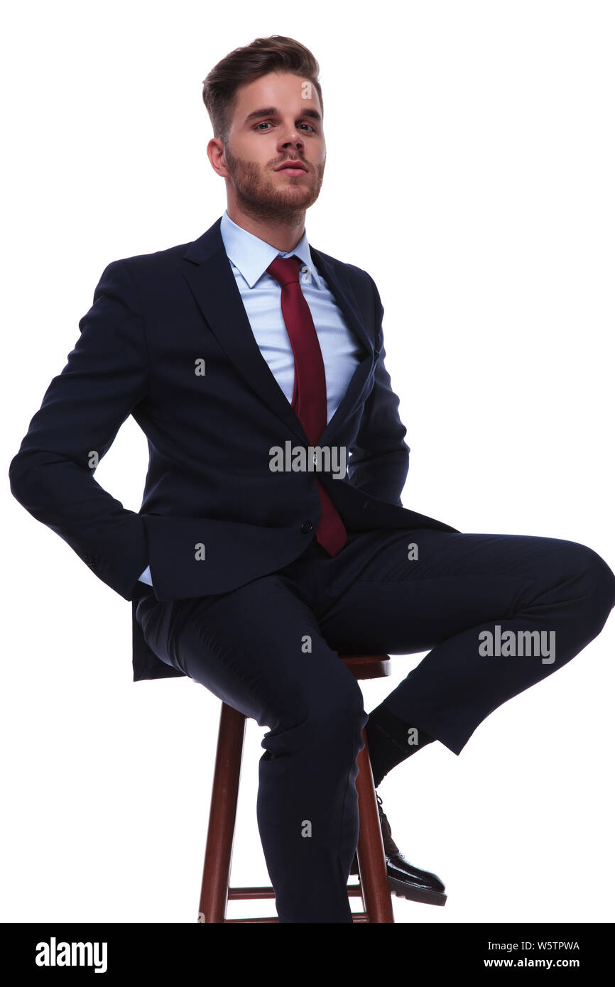 Portrait Of Proud Businessman Sitting On Wooden Stool With Hands In Pockets He Is Wearing A