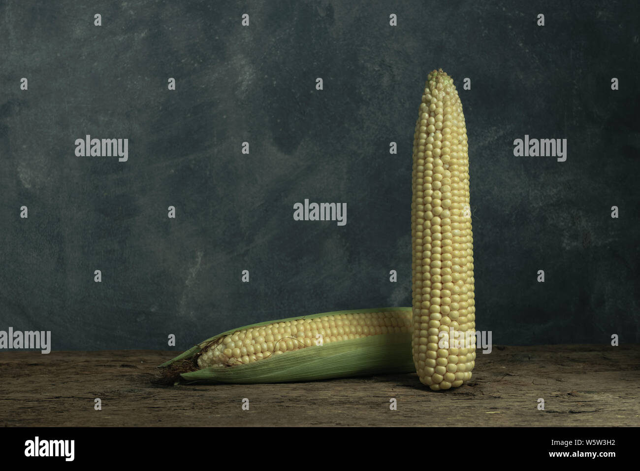 Two Fresh Sweet corn on a old oak wooden table and beautiful grey wall ...