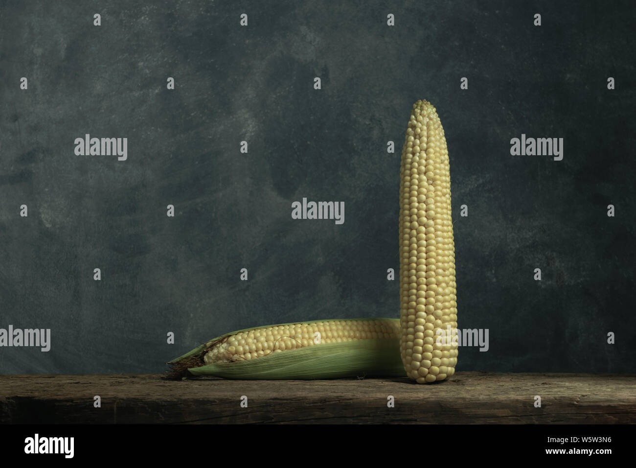 Two Fresh Sweet corn on a old oak wooden table and beautiful grey wall ...