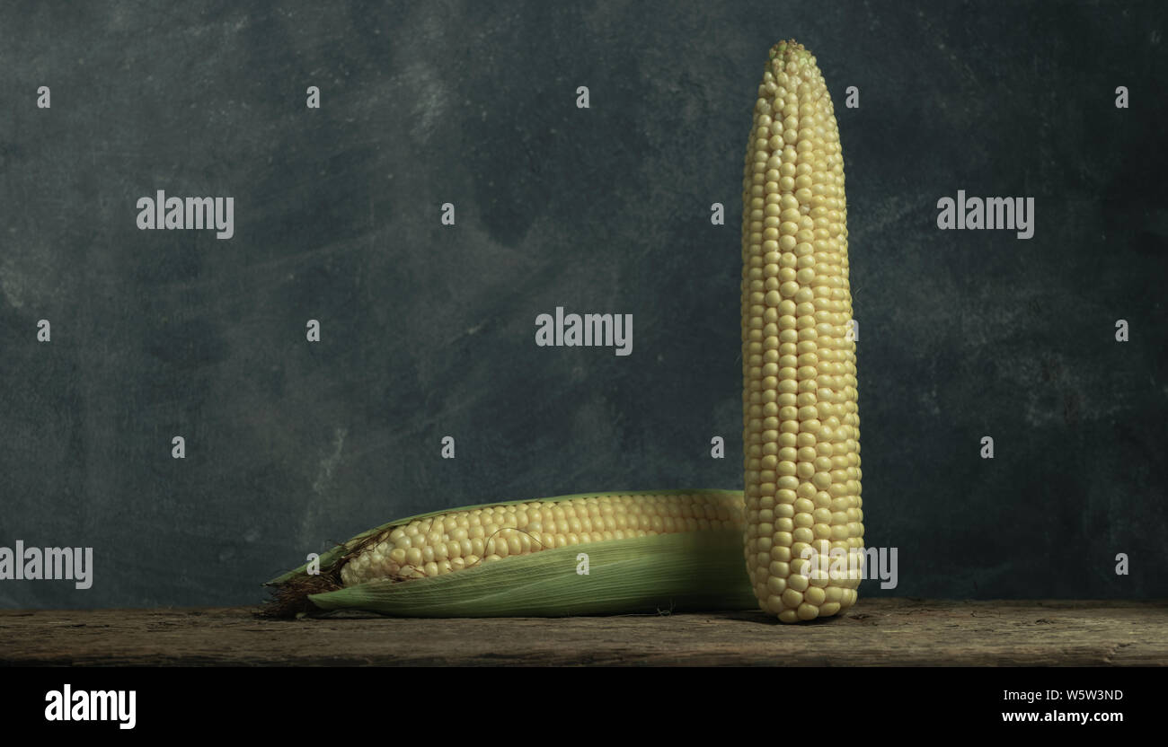 Two Fresh Sweet corn on a old oak wooden table and beautiful grey wall ...