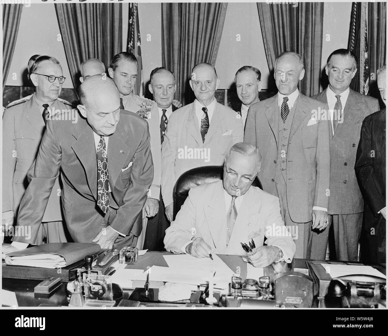 Photograph of President Truman at his desk in the Oval Office, signing ...