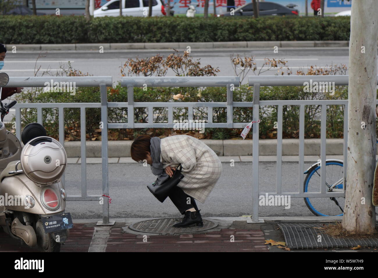 A Chinese pedestrian bends and gets through a hole to cross the road ...