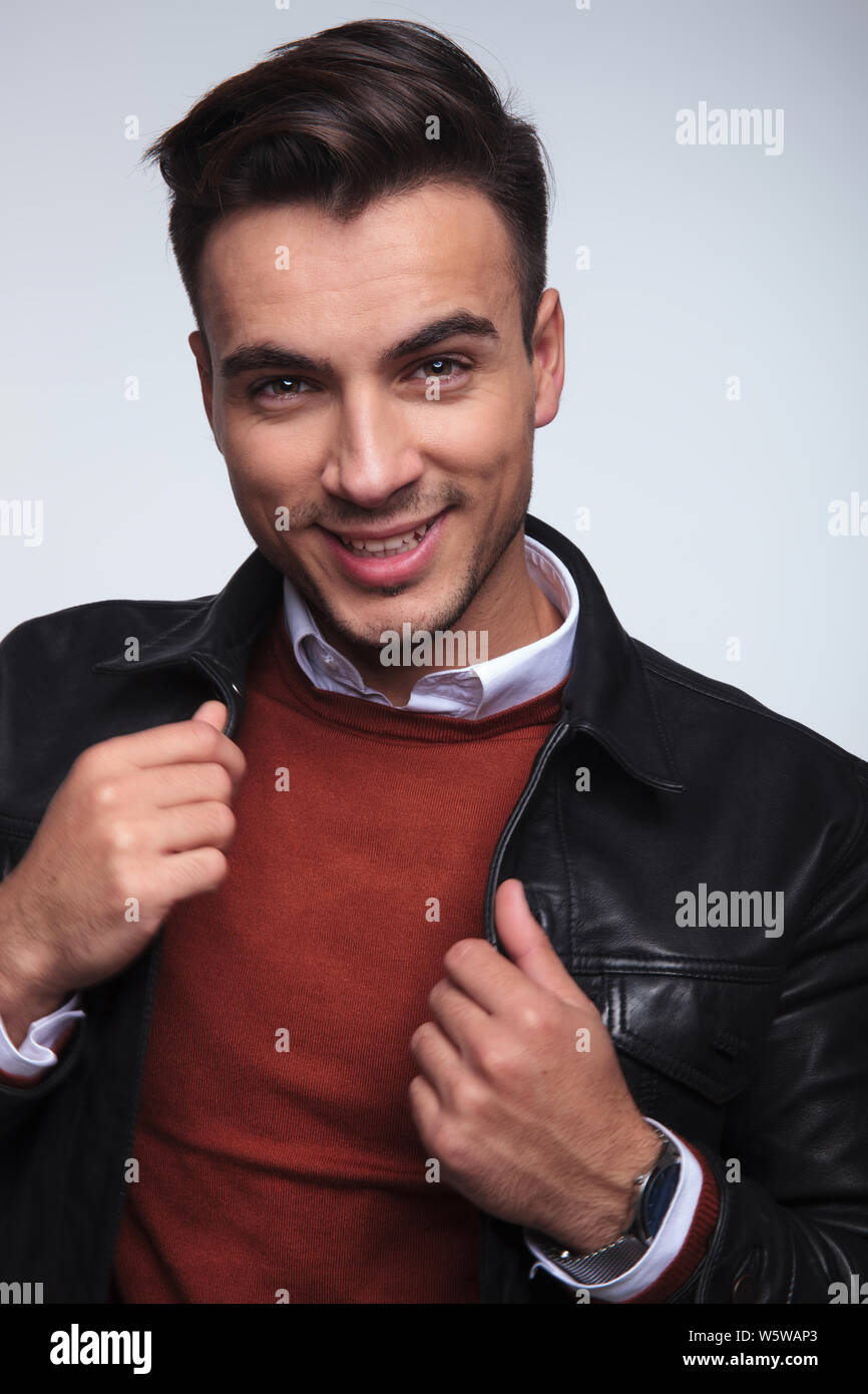 smiling young fashion man pulling his collar on light grey background ...