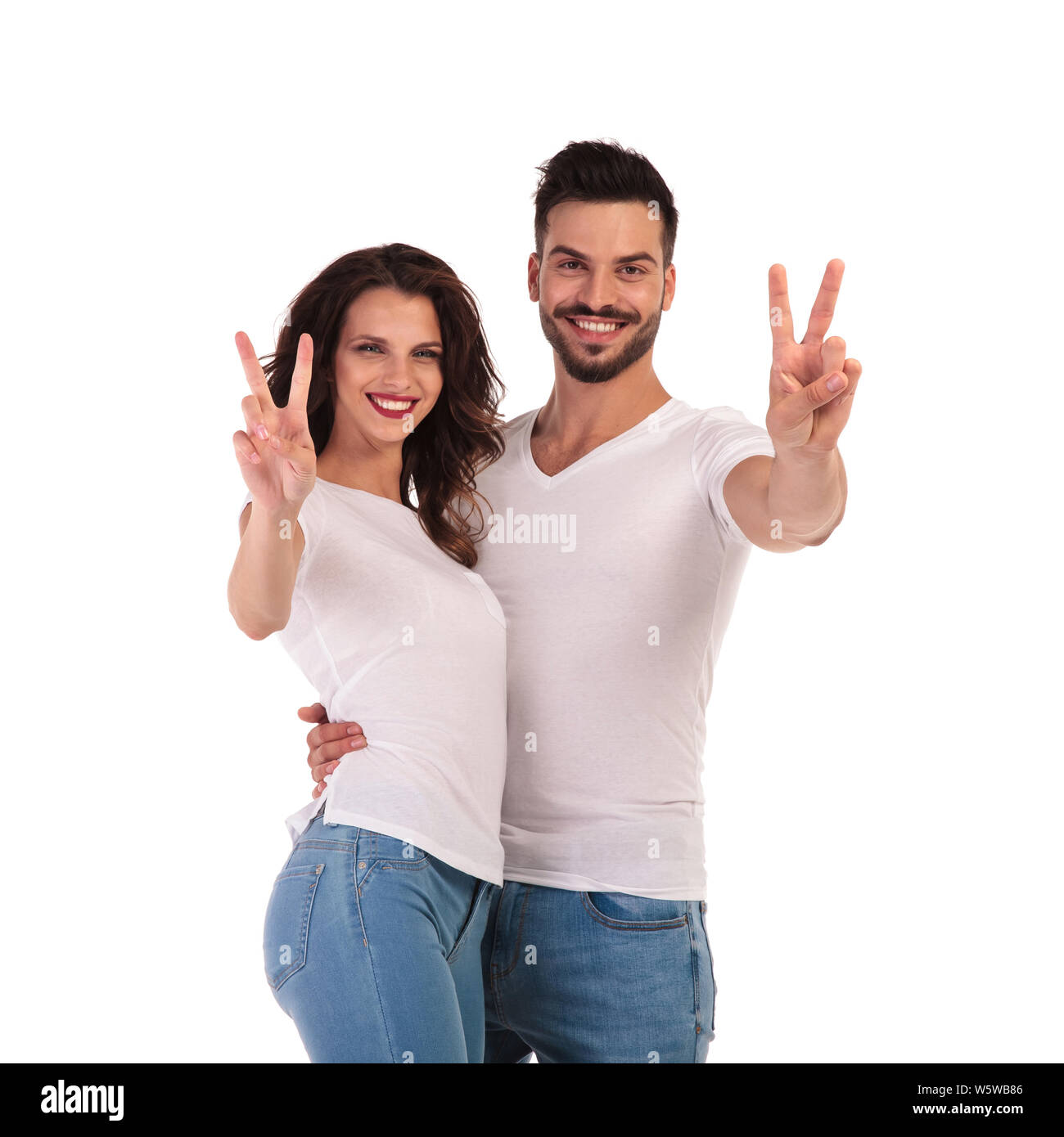 smiling young casual couple making victory or peace sign on white ...