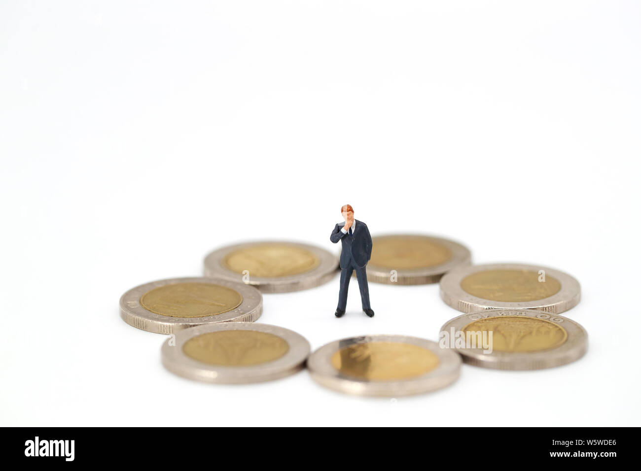 Miniature people: businessman looking around coins and thinking ...