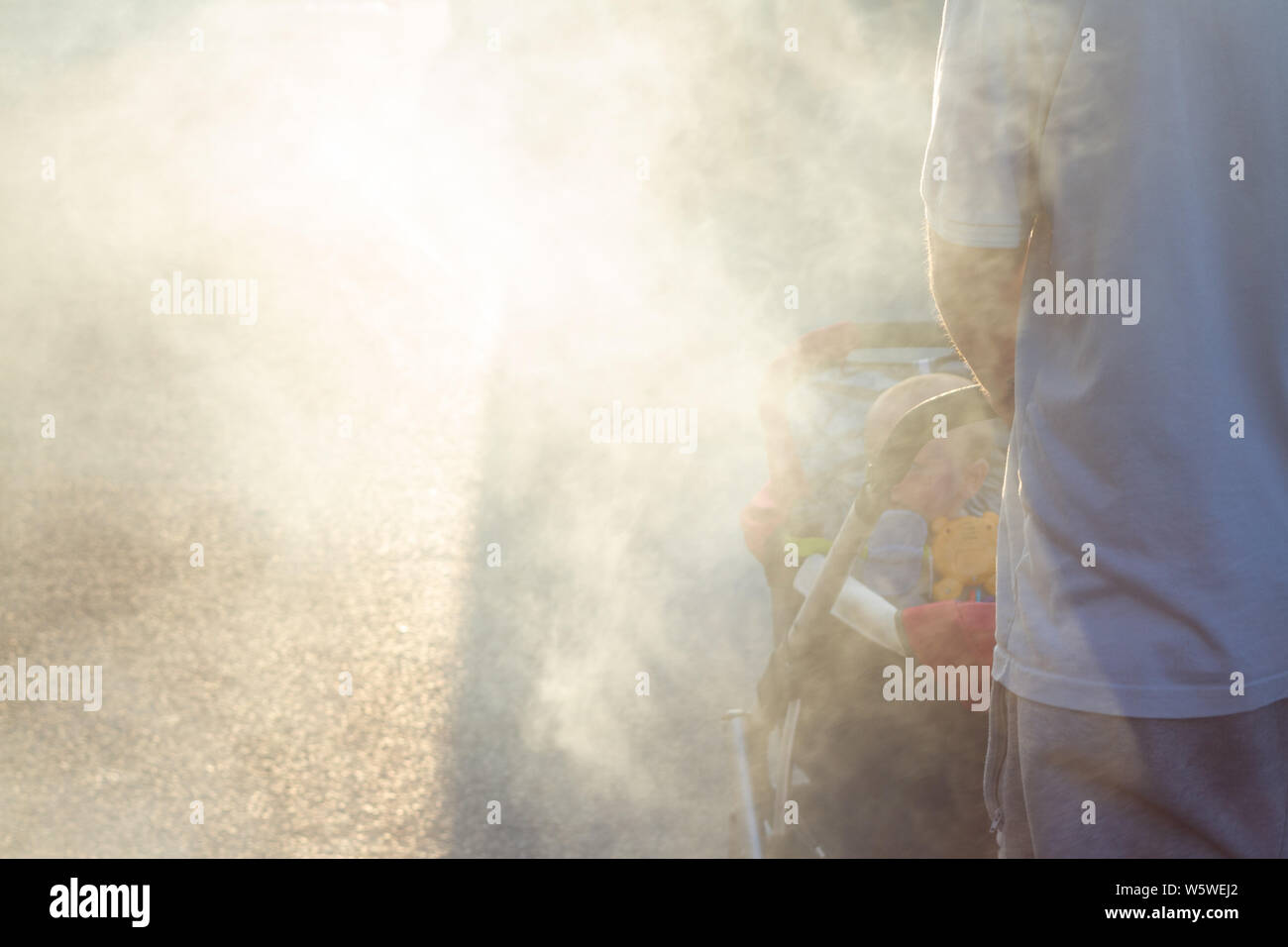 Man pushing buggy with baby trough smoke into the light seen from ...