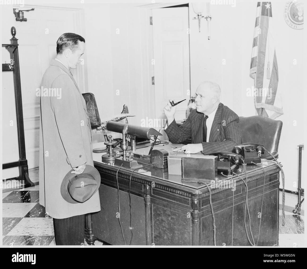 Photograph of White House receptionist William Simmons at his desk, conversing with an ...