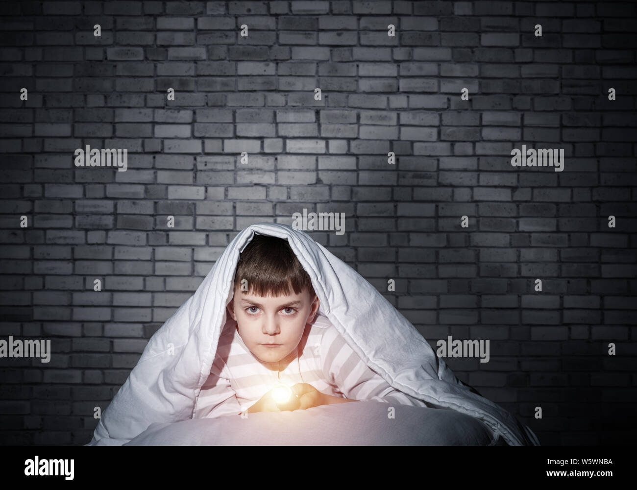Serious child with flashlight hiding under blanket. Attentive kid lying ...