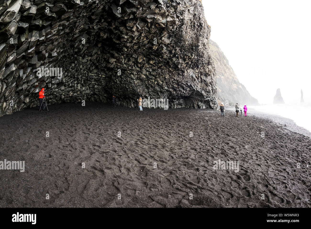 Tourists exploring rare rocky cave formations in the black sand beach ...