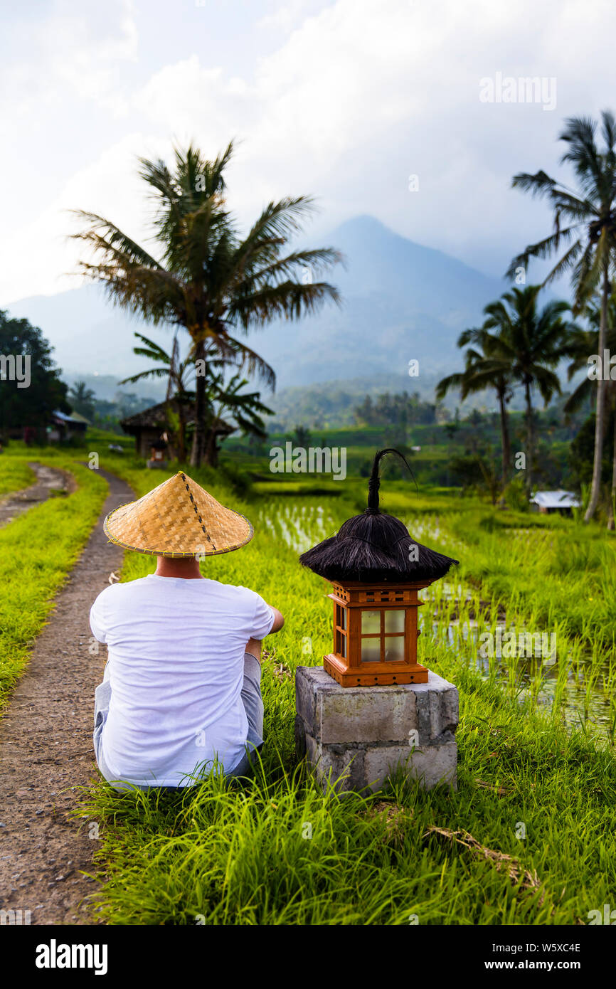 Man with traditional balinese cap by small altar at rice fields of ...