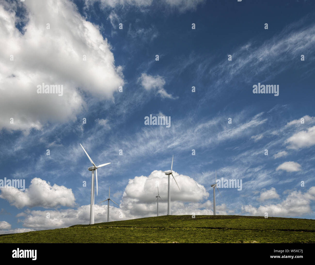 Wind farm on a green hill under a blue sky dotted with white clouds ...