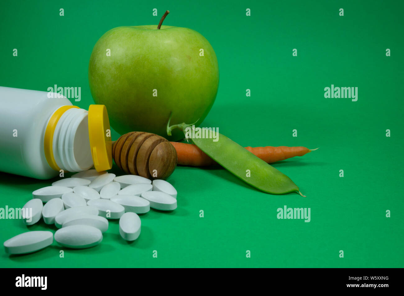 Pills spilling out of a white bottle near apple, pea pod and carrot on ...
