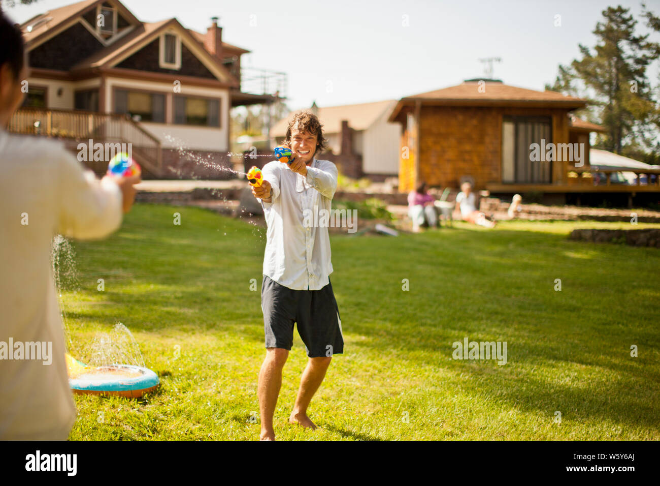 Two men having a water gun fight in a backyard Stock Photo - Alamy