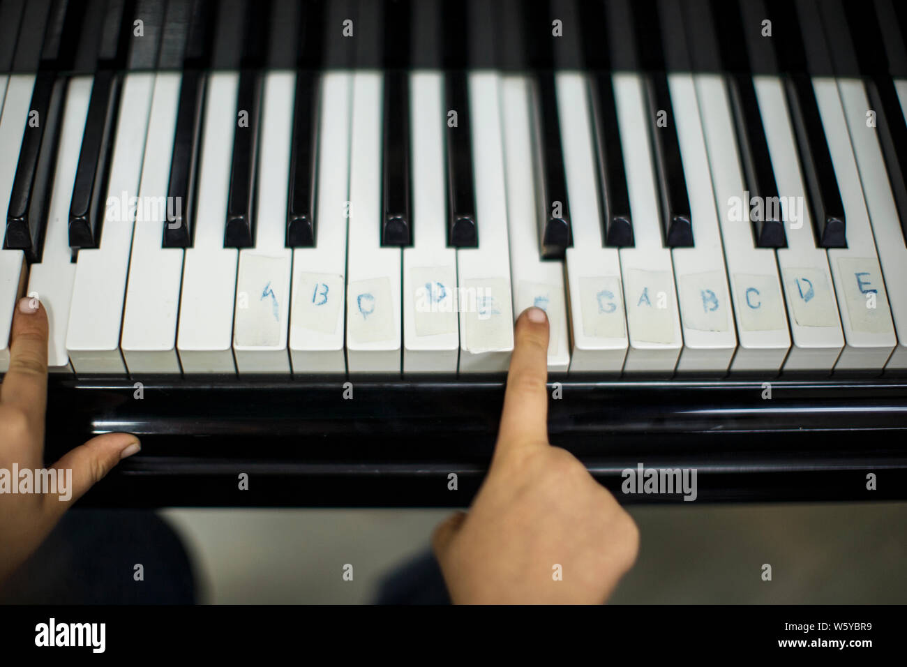 Young boy learning to play the piano helped by notes taped to the keys ...