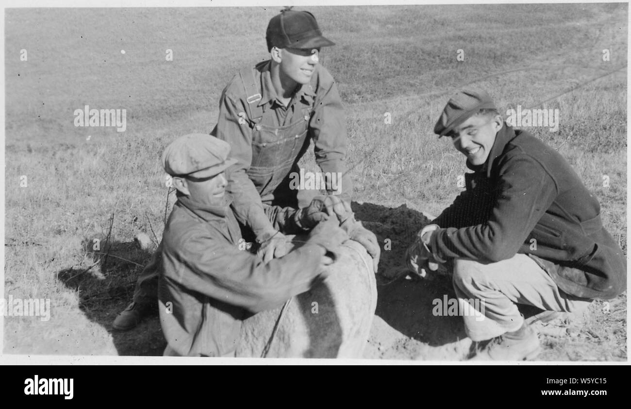 Three men try to move a boulder Stock Photo - Alamy