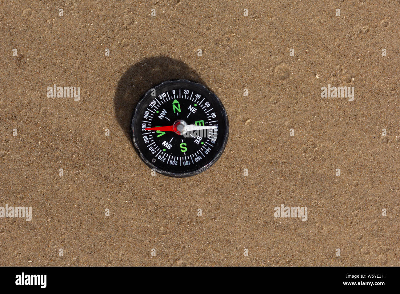 Compass pointing West laying on beach Stock Photo - Alamy